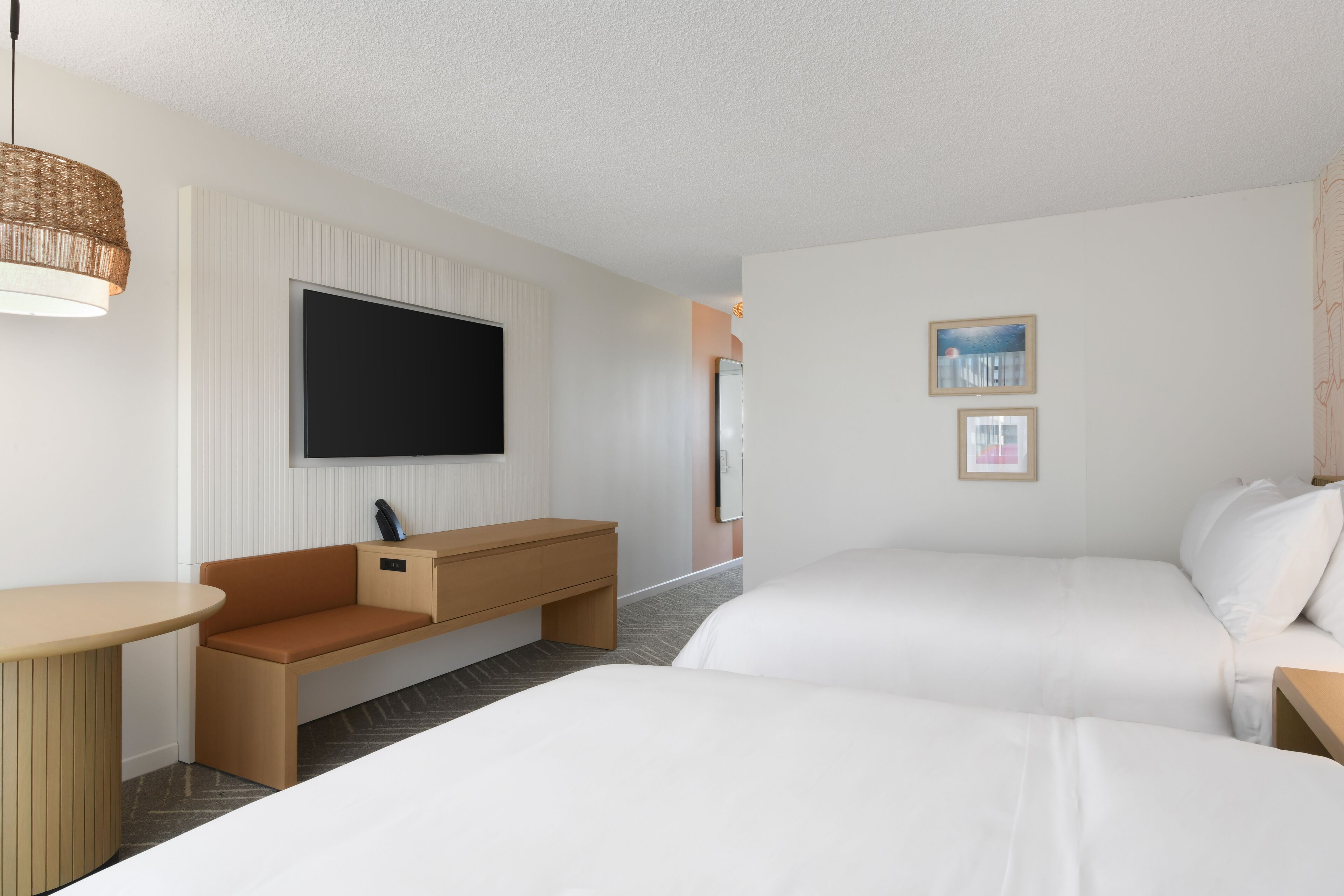 Quarto de hotel com duas camas, televisão na parede, um banco e uma mesinha.