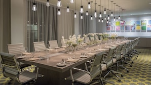 Sala de conferência com uma longa mesa preparada para uma reunião, equipada com cadeiras e um candelabro.