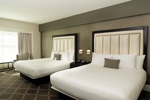 Quarto de hotel com duas camas, uma mesa e uma cadeira.