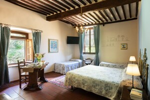 Quarto com mesa de madeira, duas camas com roupa de cama florida, um candelabro e uma janela com cortinas.