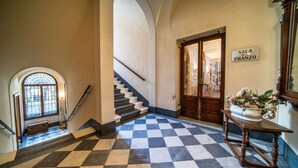 Um chão xadrez, uma escadaria, uma porta de madeira e uma placa que diz 'Sala da Pranzo'.