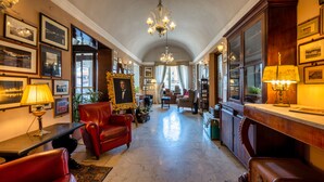 Um corredor amplo com um sofá de couro vermelho, um armário de madeira e um candelabro.