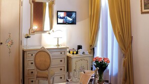 Quarto de hotel com teto de madeira, uma cama, uma escrivaninha com cadeira, toucador com espelho, televisão e janela com cortinas.