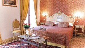 Quarto bem arrumado com cama, mesas de cabeceira, uma cadeira e uma mesa com um copo e uma garrafa.