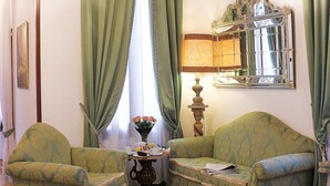 Quarto com duas poltronas verdes estampadas, teto de madeira, lustre, mesa com abajur e espelho na parede.