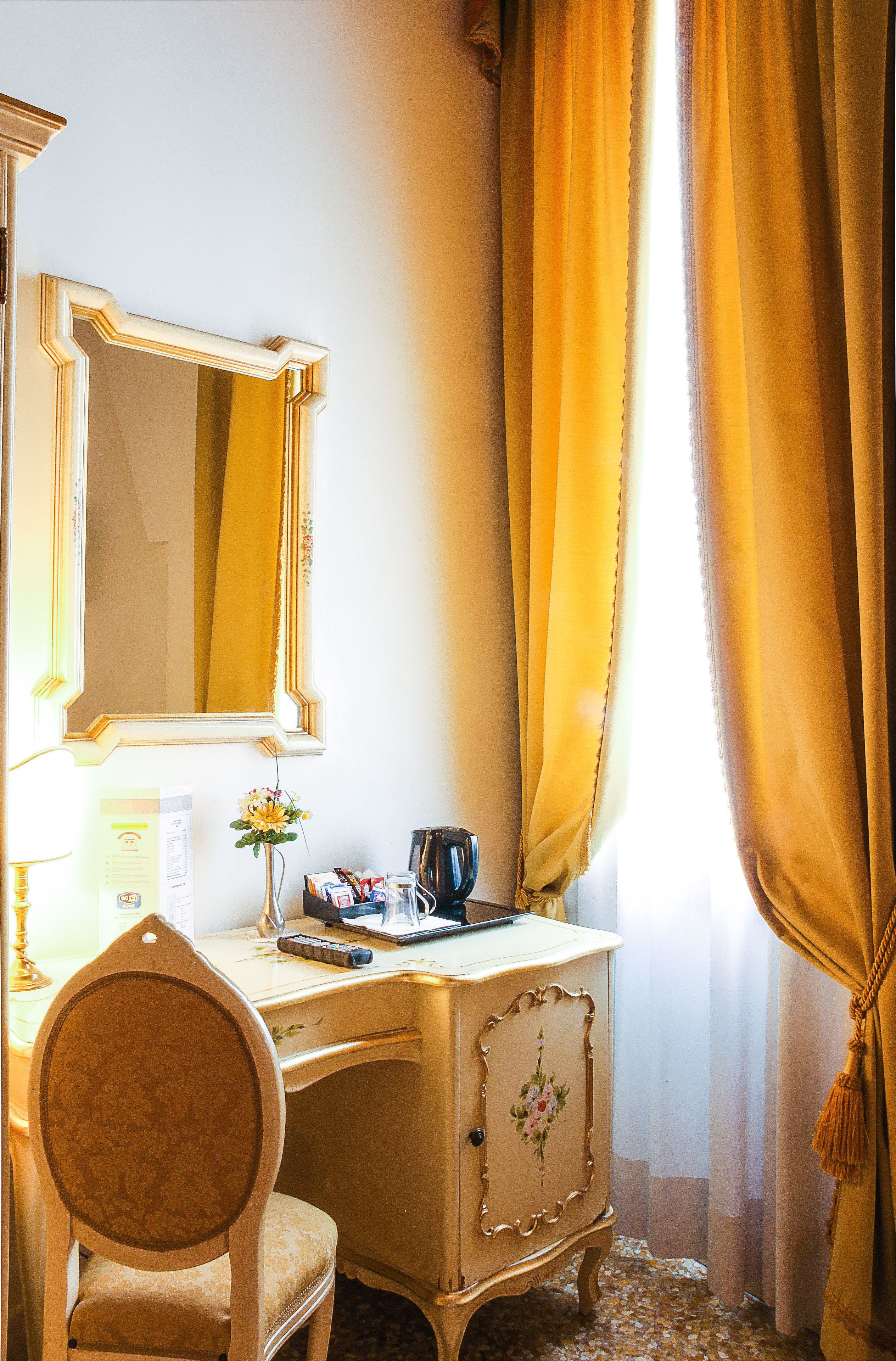 Quarto com toucador, espelho, cadeira e escrivaninha com um vaso de flores.