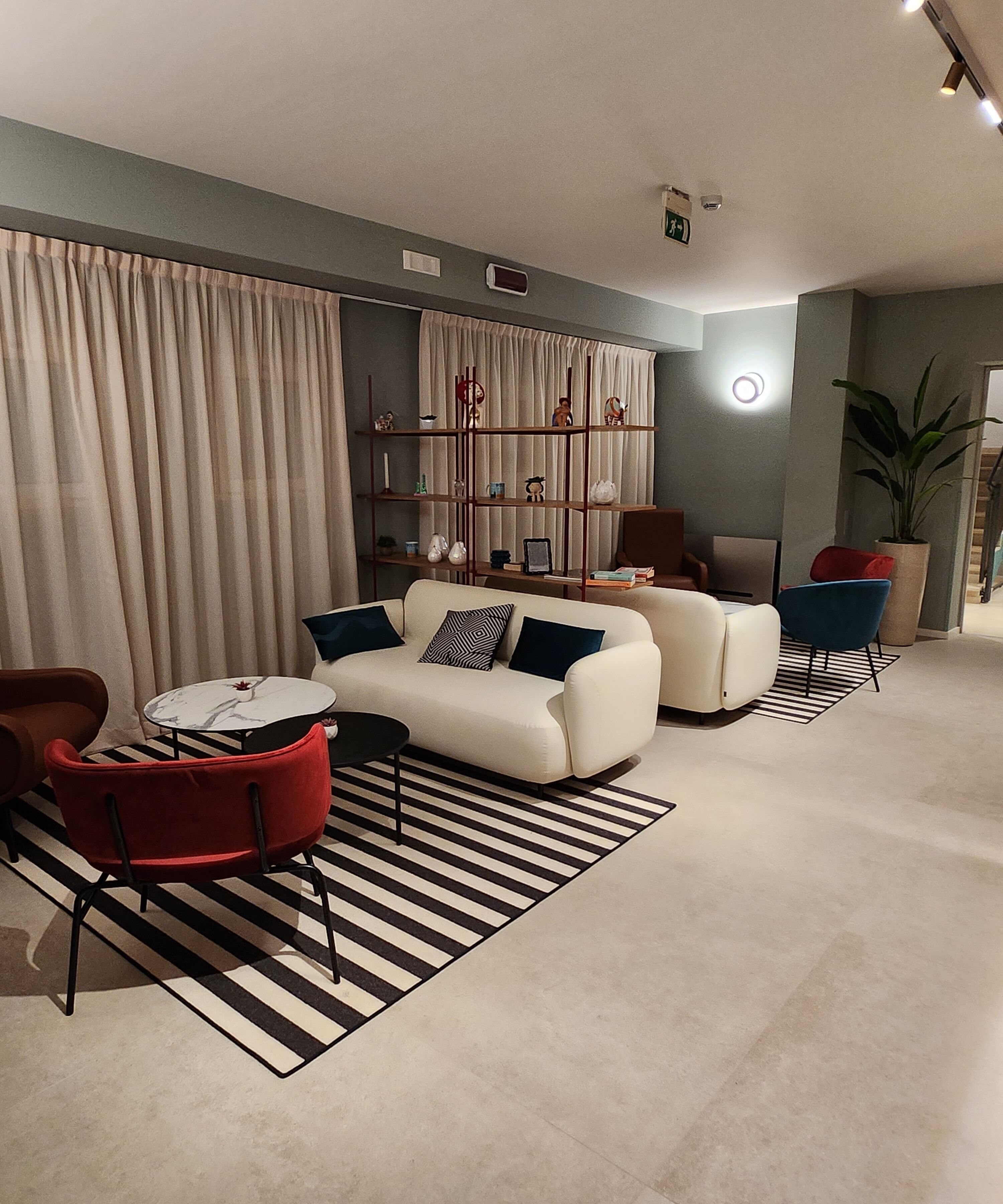 Uma sala de estar moderna com um sofá branco, cadeiras vermelhas, uma mesa redonda pequena e um tapete listrado.