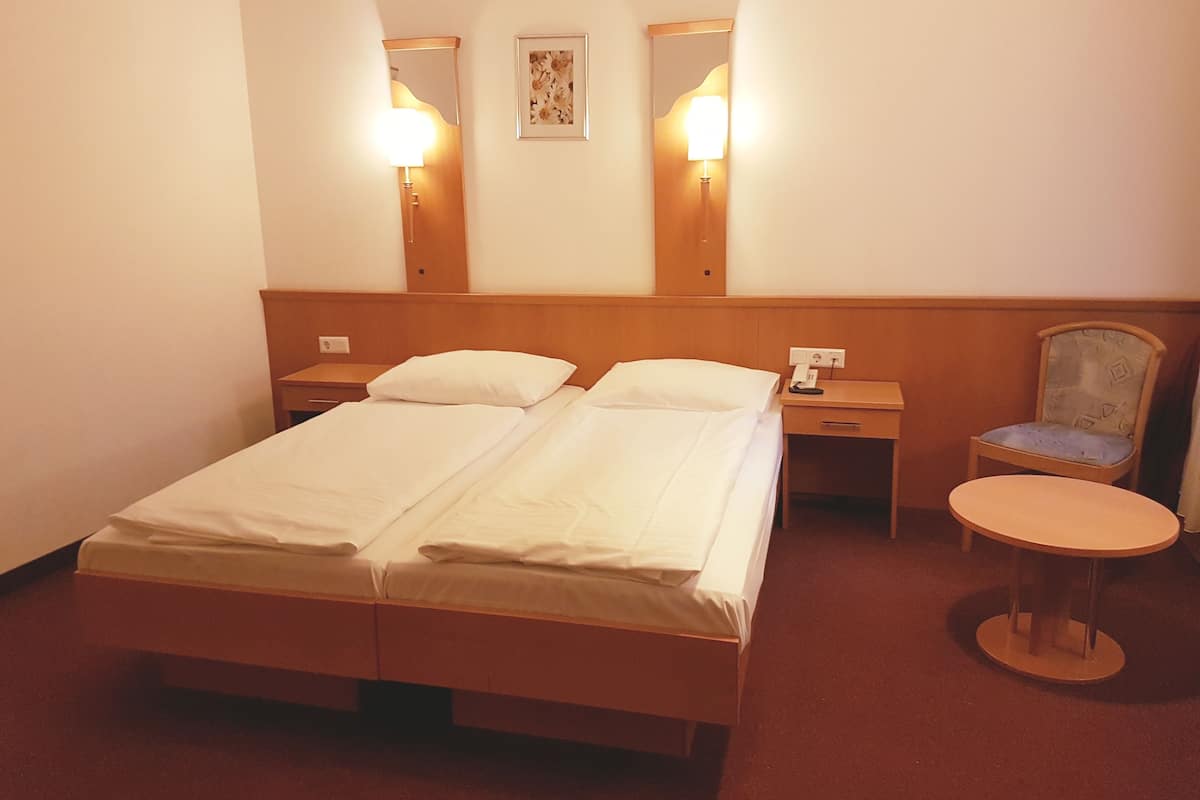 Quarto de hotel com cama de casal, mesa de cabeceira, uma cadeira, uma mesinha redonda e espelho na parede.