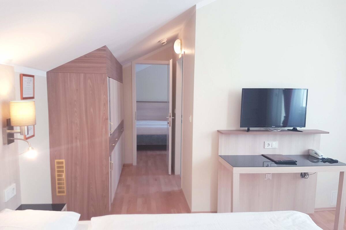 Quarto de hotel com cama, escrivaninha, televisão, telefone e luminária.