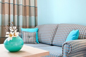 Um quarto com um sofá xadrez, um vaso azul-turquesa com flores e uma mesa de madeira.