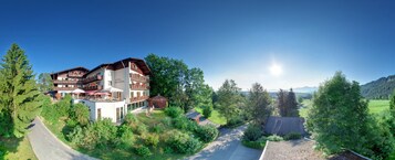Um hotel com várias varandas, uma área externa coberta e vista para o verde e montanhas ao redor.