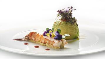 Um prato com tartare de salmão e um purê de batata coberto com folhas e flores.