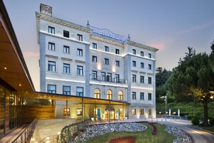 Um hotel de vários andares com entrada imponente, jardim ajardinado e fachada bem iluminada.