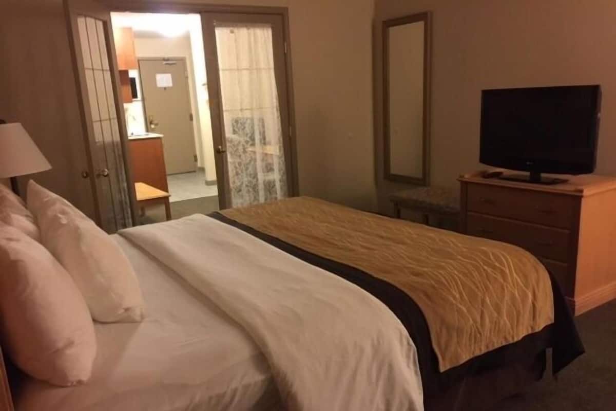 Quarto de hotel com uma cama, uma televisão sobre uma cômoda e um banheiro visível através de uma porta aberta.
