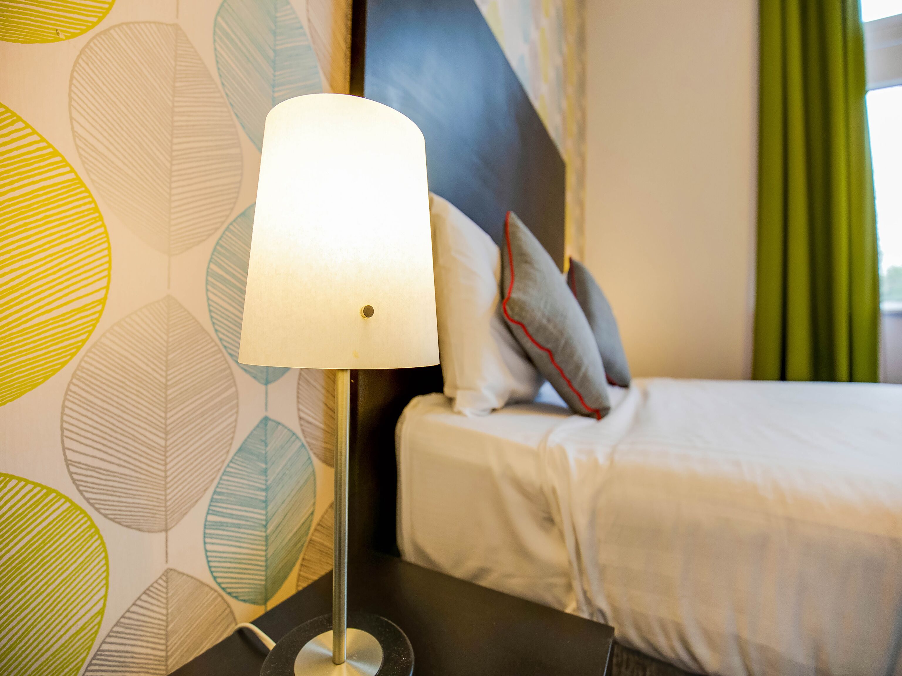 Quarto de hotel com cama, almofadas, mesa de cabeceira e luminária.