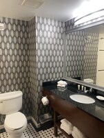 Um banheiro com papel de parede estampado, pia preta, espelho e vaso sanitário.
