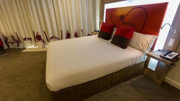 Quarto de hotel com uma cama grande, uma mesa de cabeceira com abajur e vista para a cidade pela janela.