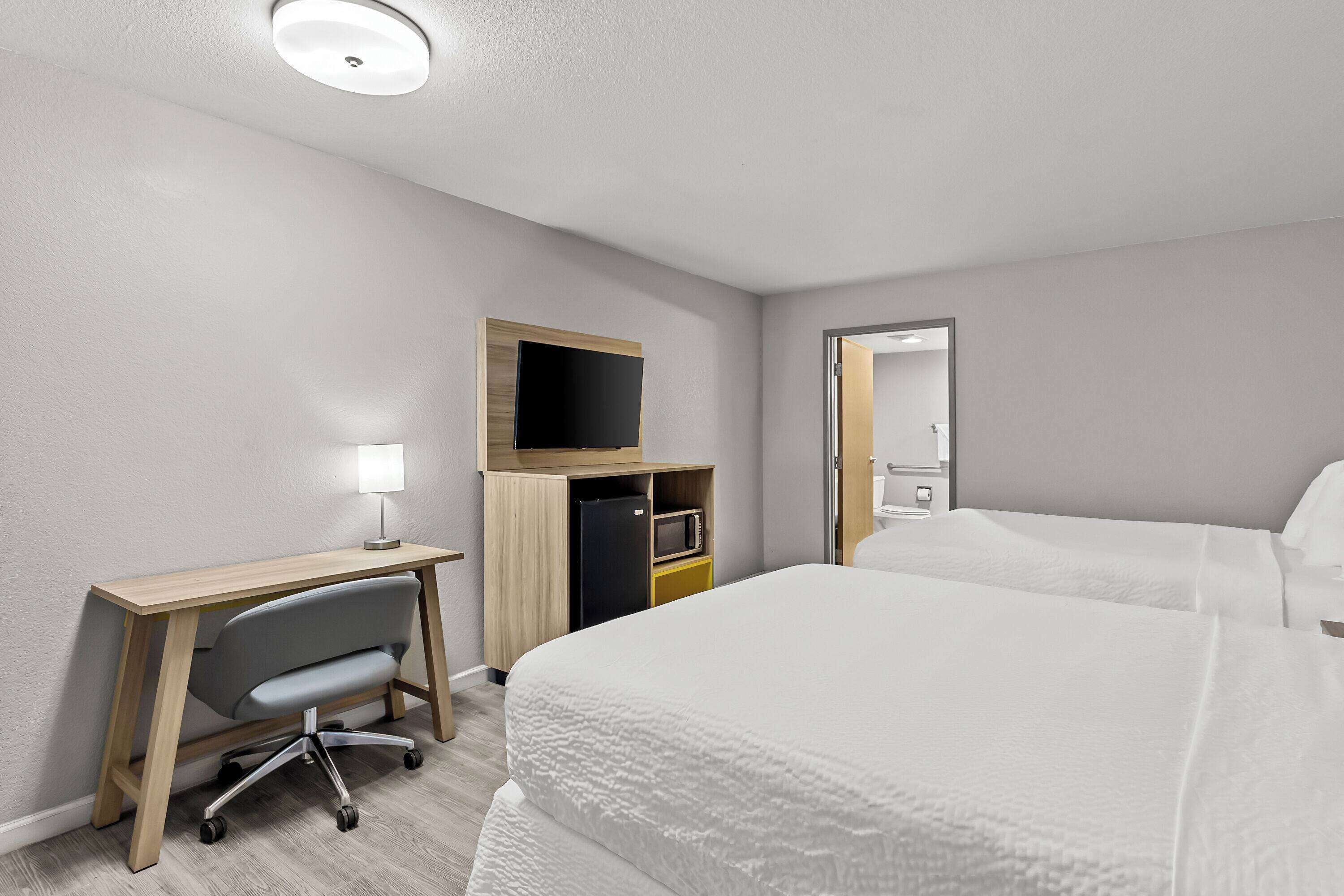 Quarto de hotel com cama, escrivaninha com cadeira, televisão e micro-ondas.