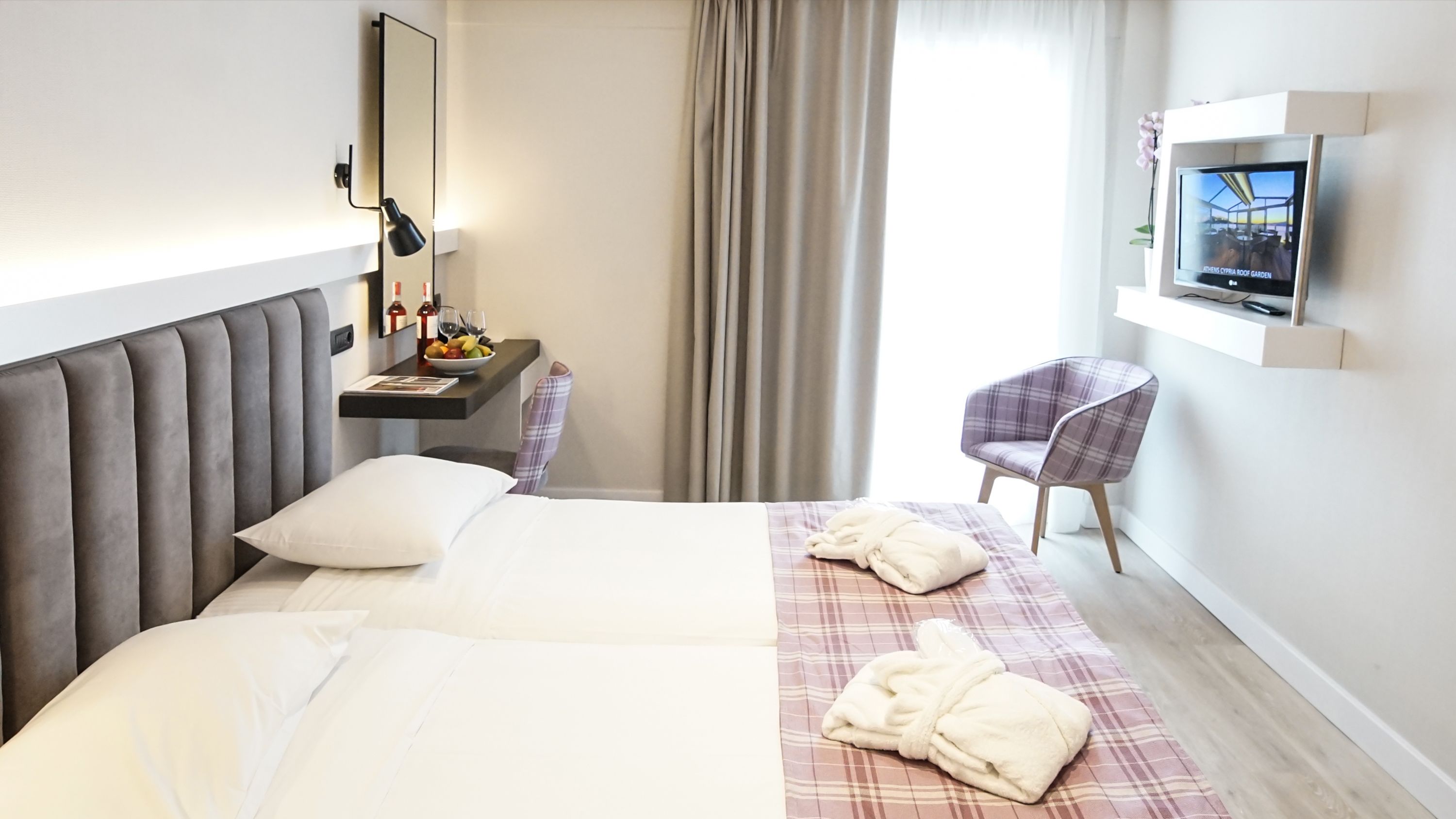 Quarto de hotel com uma cama grande, uma mesa de cabeceira com abajur, uma cadeira, uma TV e uma janela com cortinas.