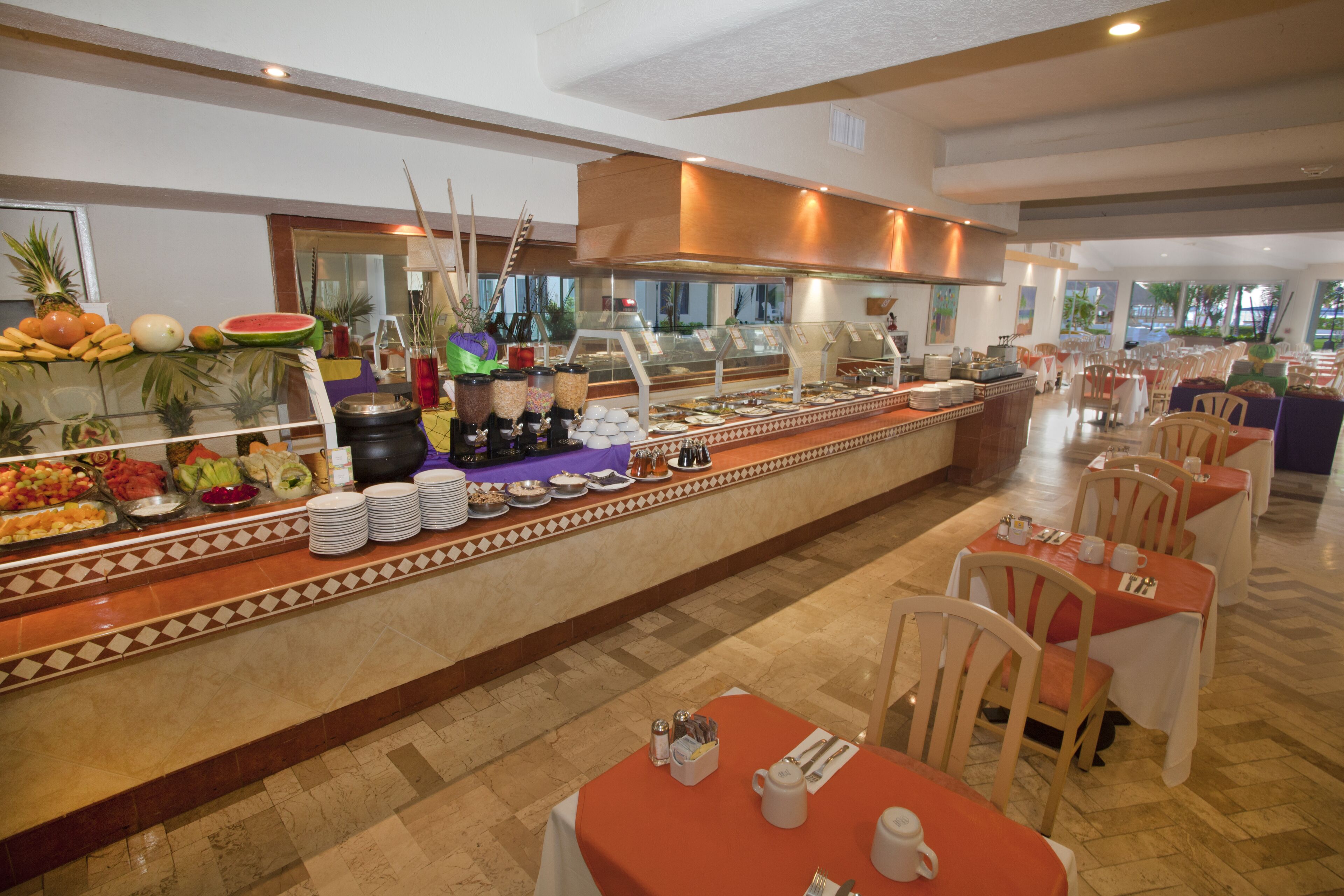 Uma área de buffet com diversos tipos de comida e um espaço de estar com mesas e cadeiras.