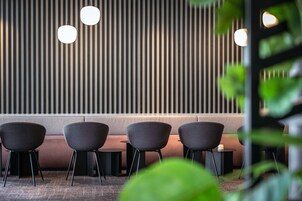 Um interior moderno com uma fileira de cadeiras escuras, um banco estofado e uma parede com listras verticais e luminárias pendentes.