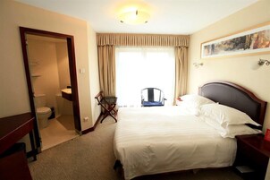 Quarto de hotel com cama, cadeira, escrivaninha e banheiro.