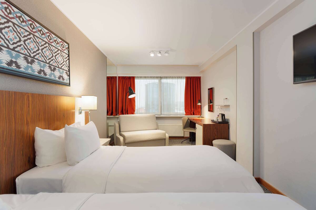 Quarto de hotel com uma cama grande, uma escrivaninha, uma cadeira e uma televisão.