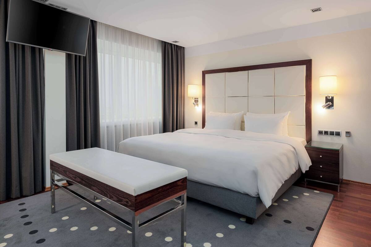 Quarto de hotel com uma cama grande, mesas de cabeceira, escrivaninha e televisão.