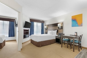 Quarto de hotel com cama, escrivaninha, cadeiras, televisão e obras de arte.