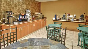 Uma área de pequeno-almoço de hotel com estação de café, mesas e cadeiras, e chão em azulejos.