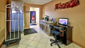 Um saguão de hotel com balcão de recepção, computador e carrinho de metal.