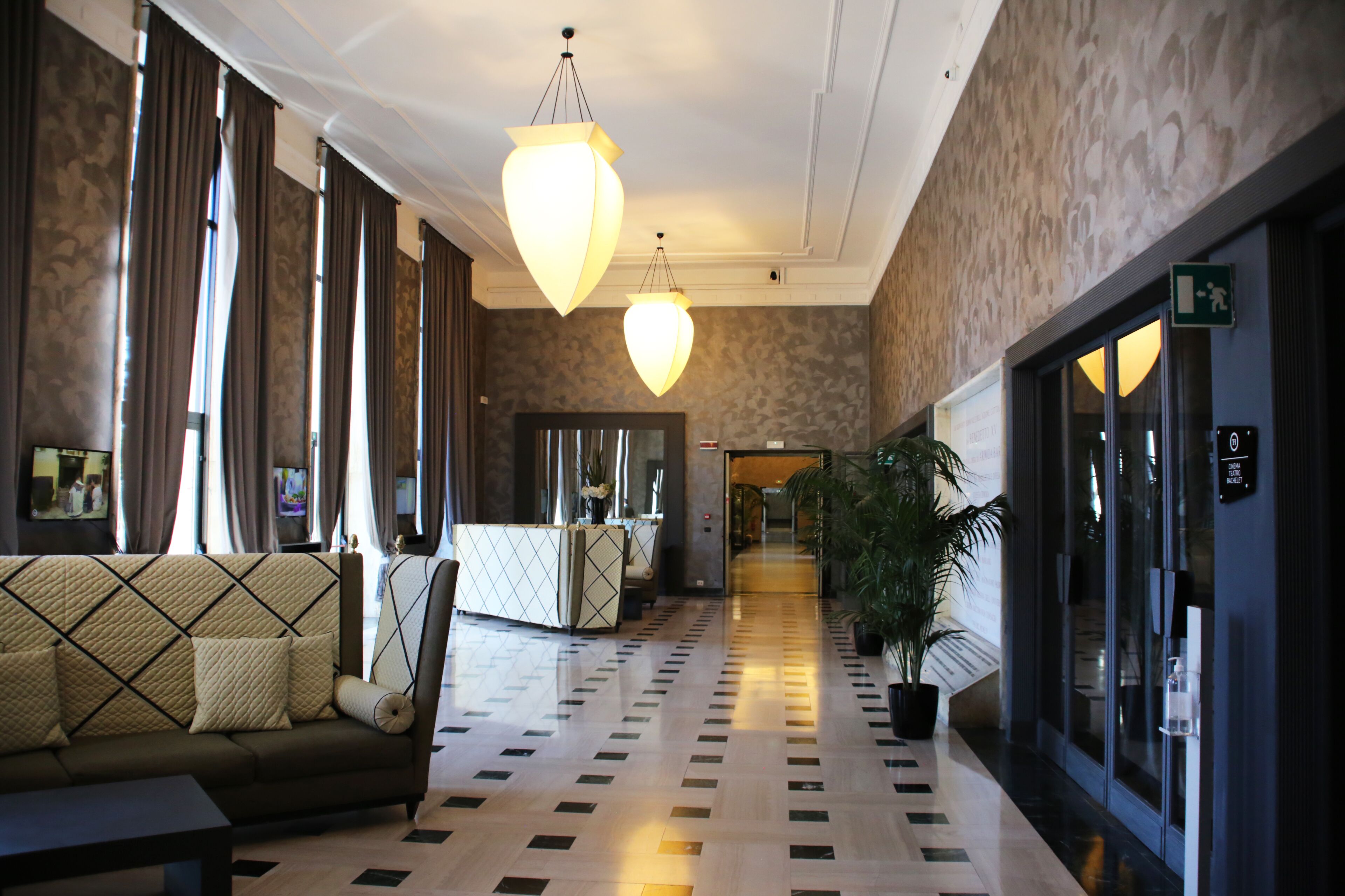 Um saguão de hotel com balcão de recepção, área de estar e corredor que dá acesso a outros quartos.