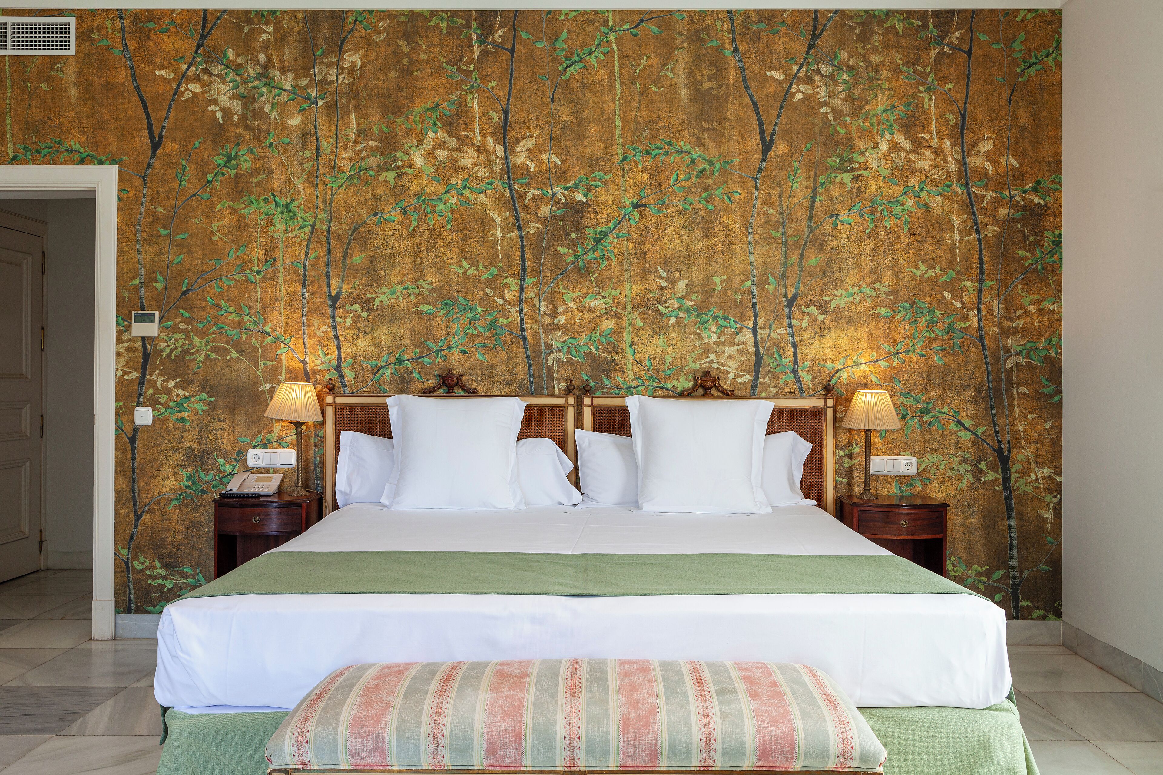 Quarto de hotel com uma cama grande, duas mesas de cabeceira e um mural na parede.