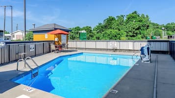 Piscina retangular com uma escada de metal de um lado, uma área cercada com um pequeno edifício e um contentor de lixo verde ao fundo.