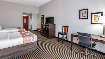 Quarto de hotel com cama, escrivaninha com cadeira, televisão e obras de arte nas paredes.