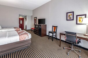 Quarto de hotel com cama, escrivaninha com cadeira, televisão e obras de arte nas paredes.