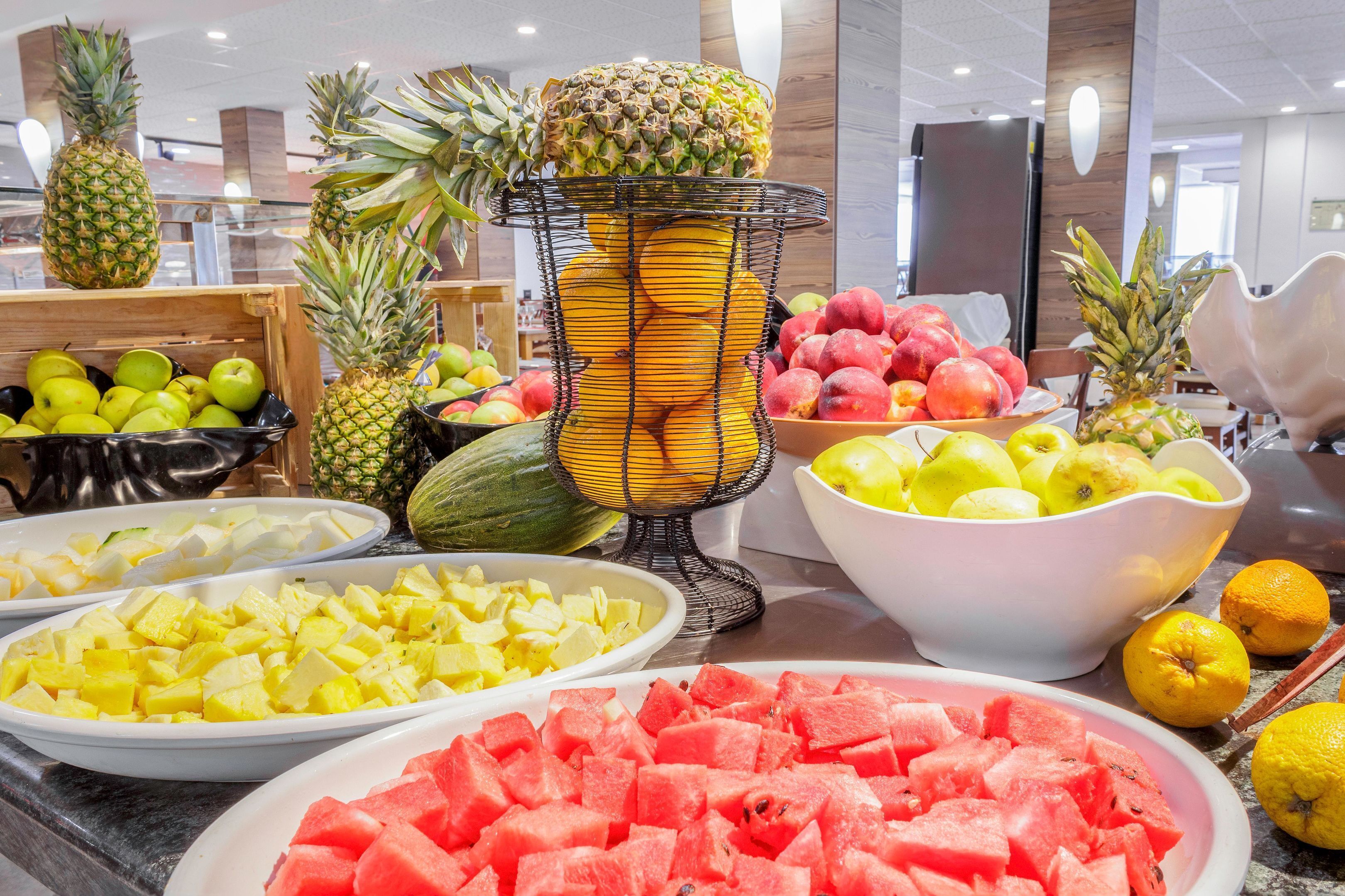 Um buffet com diversas frutas e vegetais, incluindo abacaxis, maçãs e melancia.