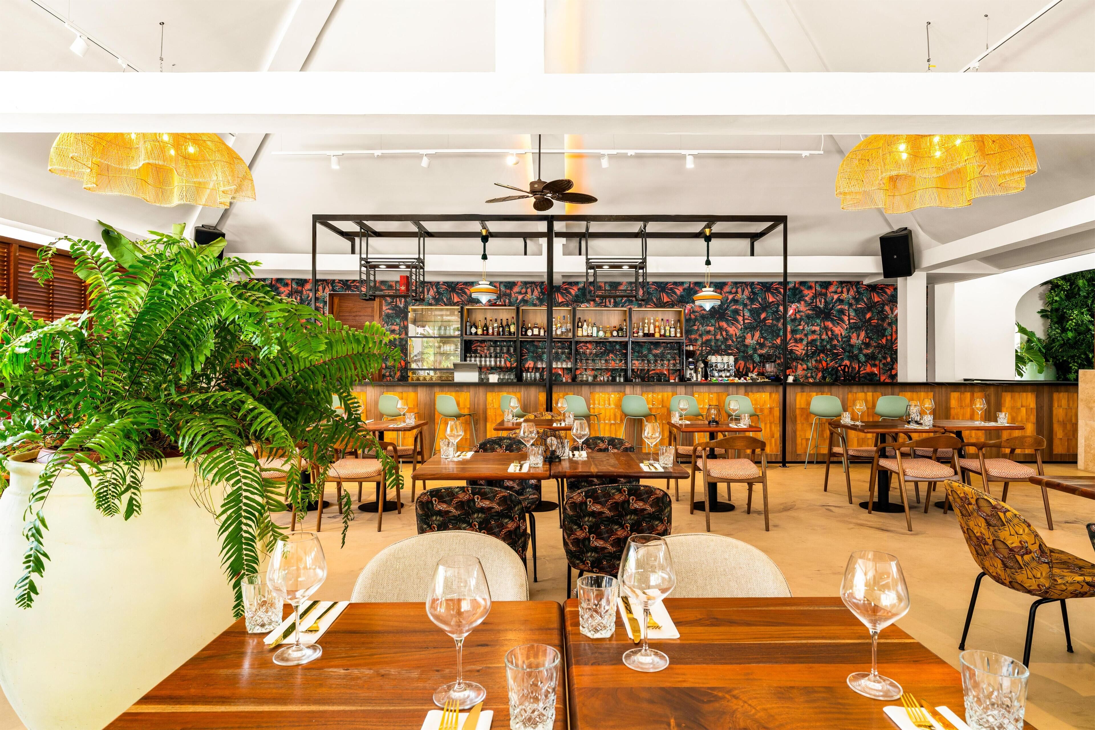 Um restaurante com mesas e cadeiras de madeira e um espaço de bar com prateleiras cheias de garrafas.