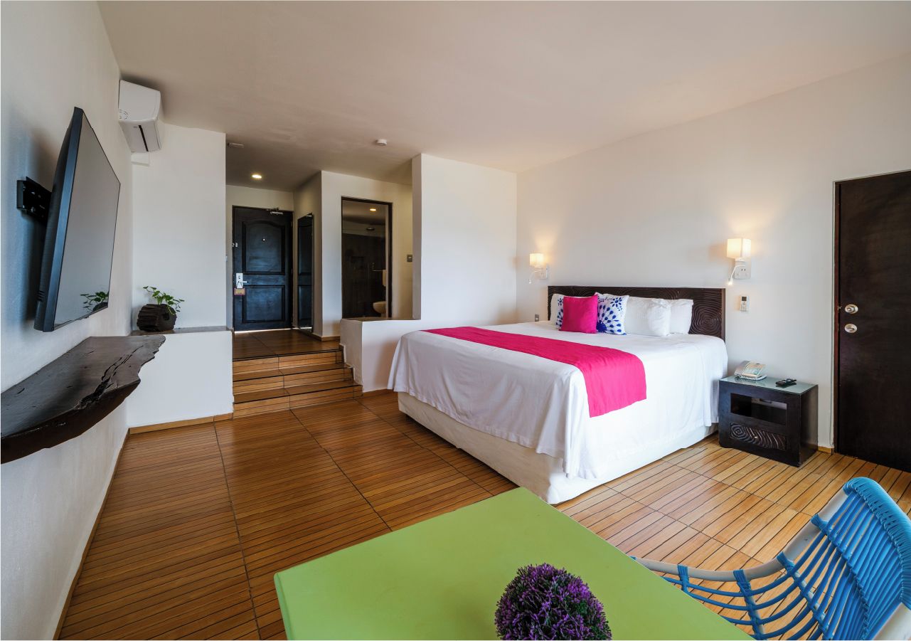 Quarto de hotel com cama, mesa de cabeceira, cadeira e televisão na parede.