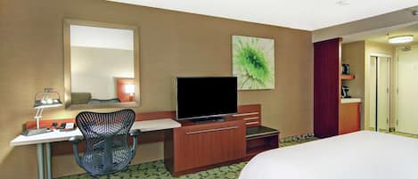 Quarto de hotel com cama, escrivaninha, cadeira, televisão e espelho.