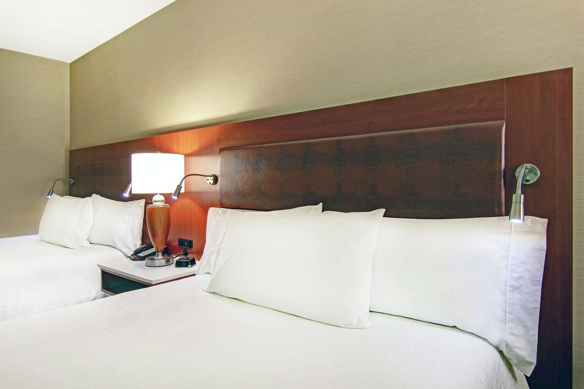Quarto de hotel com duas camas, uma mesa de cabeceira com abajur e um telefone.