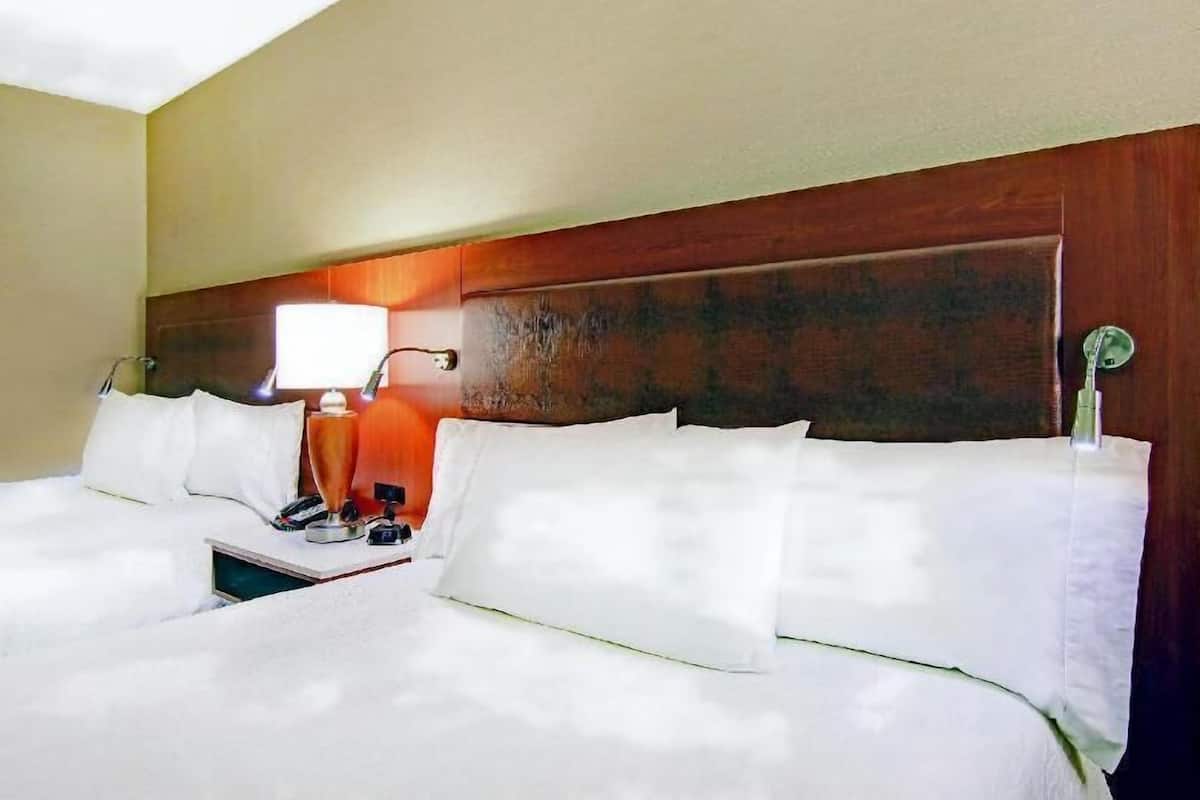 Quarto de hotel com uma cama grande, uma mesa de cabeceira com abajur e um painel de cama de madeira.