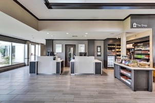 A modern reception area with a counter, a refrigerated display case, and a section labeled "The Shop" with various products.