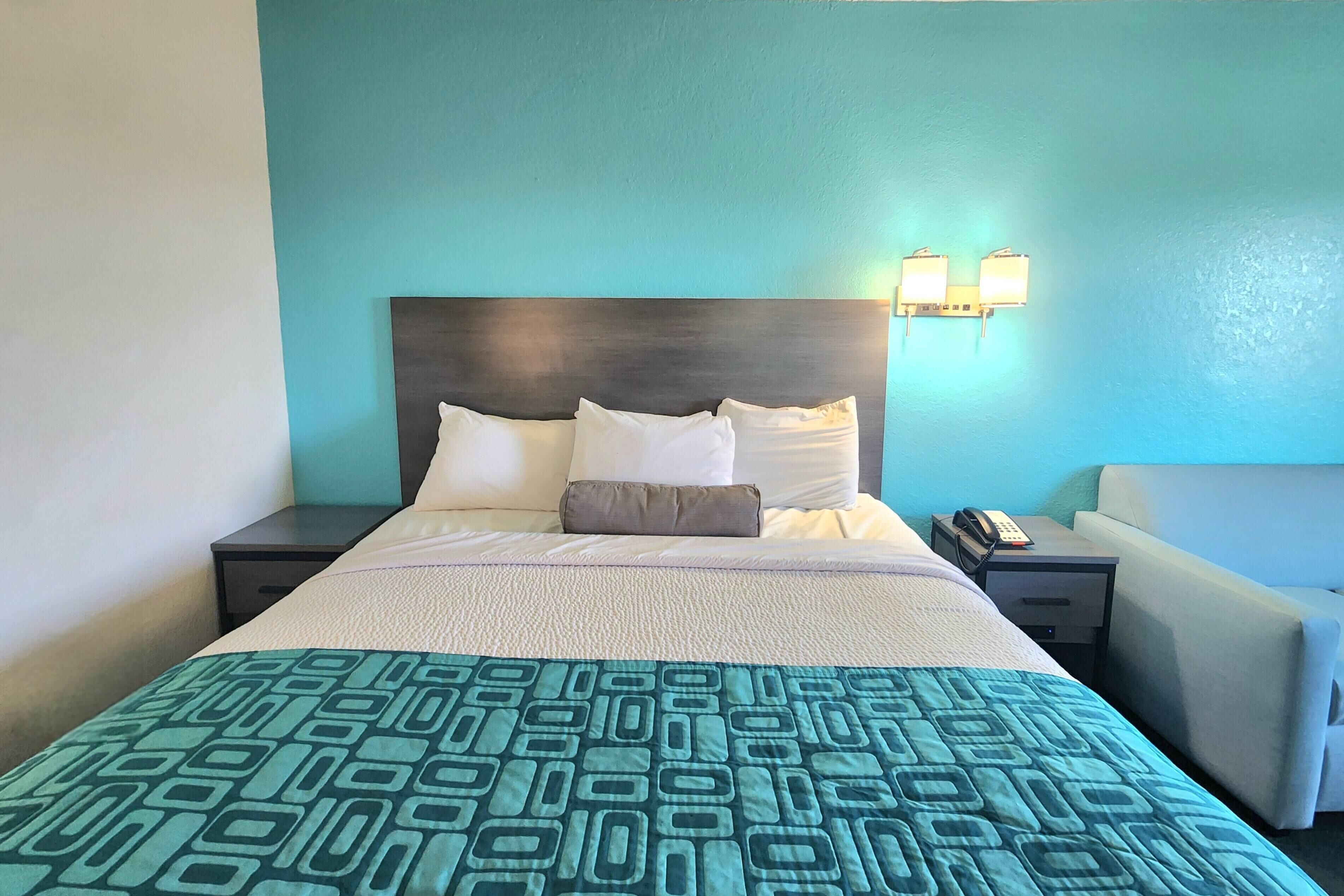Cama bem arrumada com colcha estampada, cabeceira escura e duas luminárias de mesa.