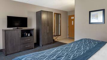 Quarto de hotel com cama, televisão, guarda-roupa e um quadro na parede.