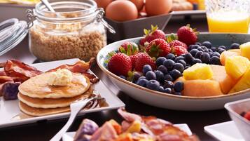 Uma mesa de café da manhã com panquecas, bacon, ovos e diversas frutas.