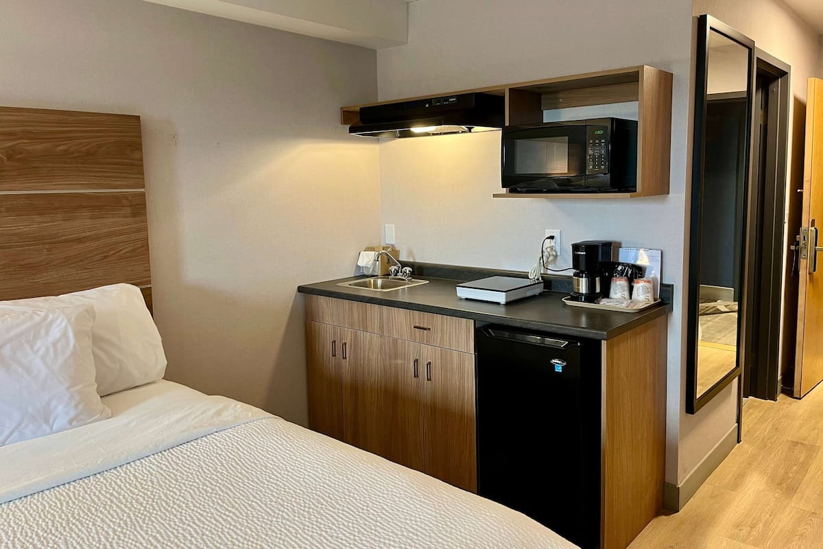 Quarto de hotel compacto com uma cama, uma pequena cozinha equipada com micro-ondas, cafeteira e máquina de lavar loiça.