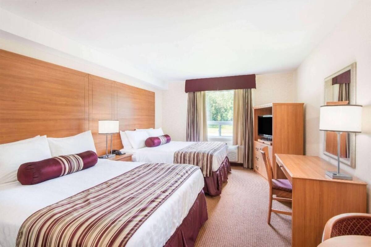 Quarto de hotel com duas camas, uma escrivaninha, televisão e janela com cortinas.