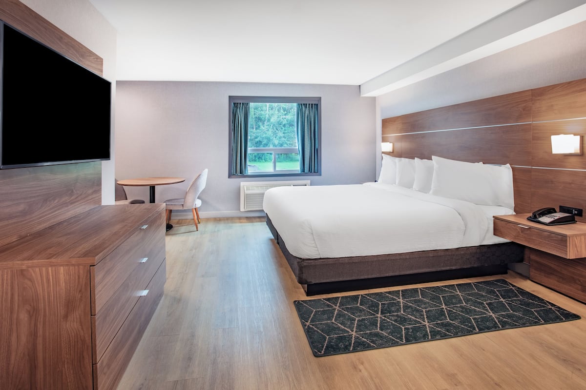 Quarto de hotel moderno com cama grande, escrivaninha, cadeira, televisão e janela com cortinas.