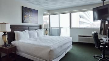 Quarto de hotel com uma cama grande, uma mesa com computador, televisão e janela com vista para edifícios.